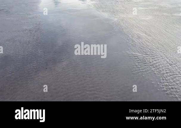Black sand beach with water reflecting blue sky and clouds. Stepping on ...