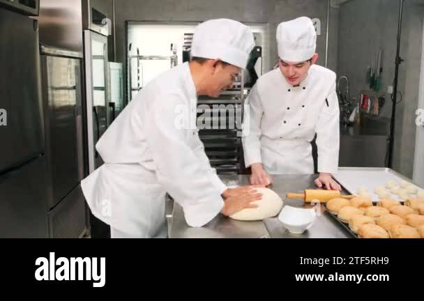 Two professional Asian male chefs in white cook uniforms and aprons are ...