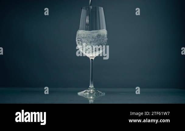 Bubbling water pouring glass at gray background closeup. Crystal clear liquid filling beautiful ...