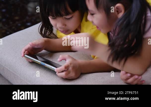 Two Sisters Are Playing Online Games On Their Smartphones Sitting On