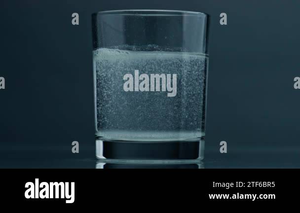 Air bubbles rising glass surface closeup. Acid fluid in transparent cup at dark background ...