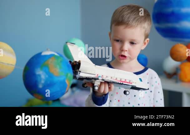 Cute boy is playing with toy space shuttle, flying in space among ...