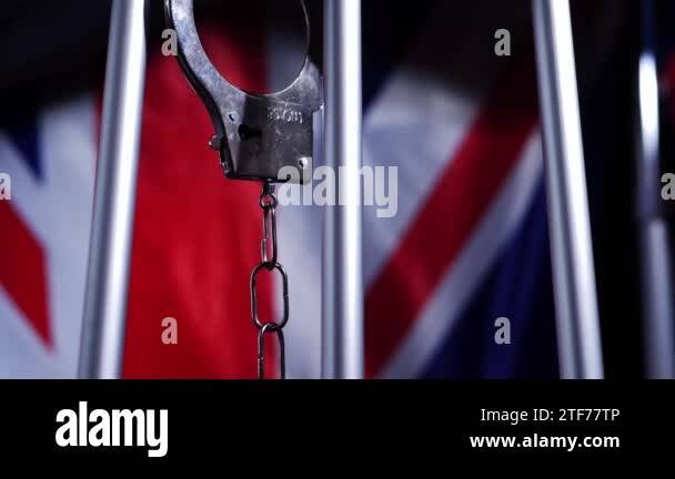 Handcuffs swing on prison bars with Union jack British flag background ...