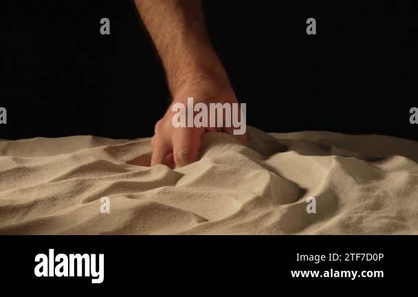 Male hand squeezing and spilling a handful of dry sand on black studio ...