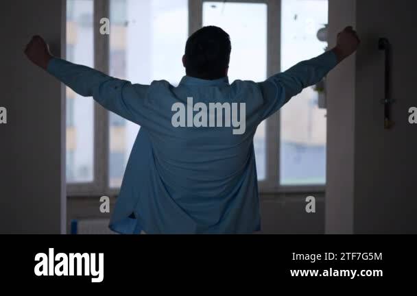 Back view silhouette of young man stretching looking out the window in ...