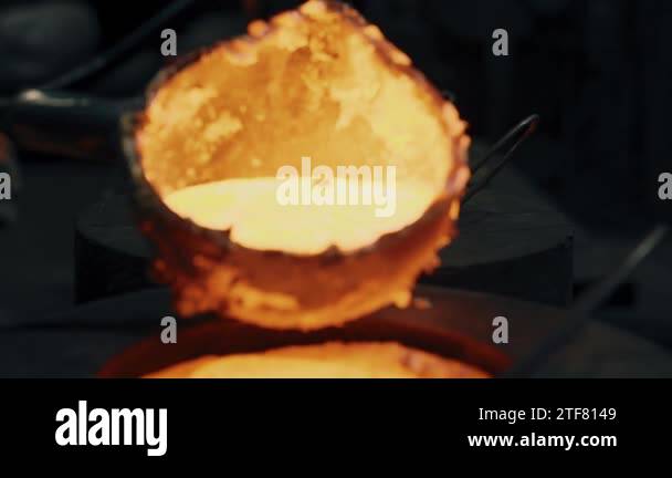 Bright molten metal from a melting pot is poured into molds. Camera ...