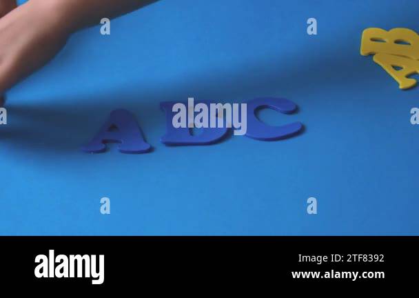 Childs hand playing with letters of the alphabet. Blue-yellow letters ...