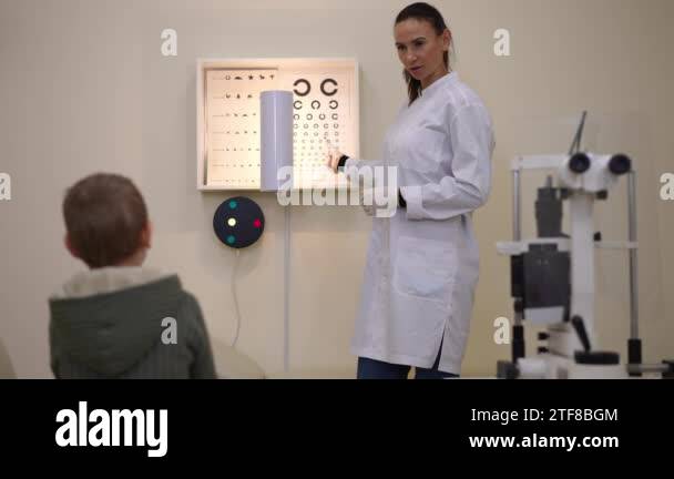 Beautiful positive doctor standing at eye sight test chart pointing ...
