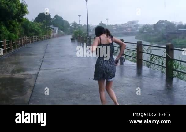 A girl is running in heavy rain at the riverside, gray concrete cloudy ...