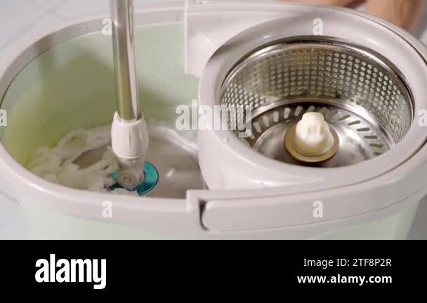 Woman holding mop with microfiber head spinning water in the bucket ...