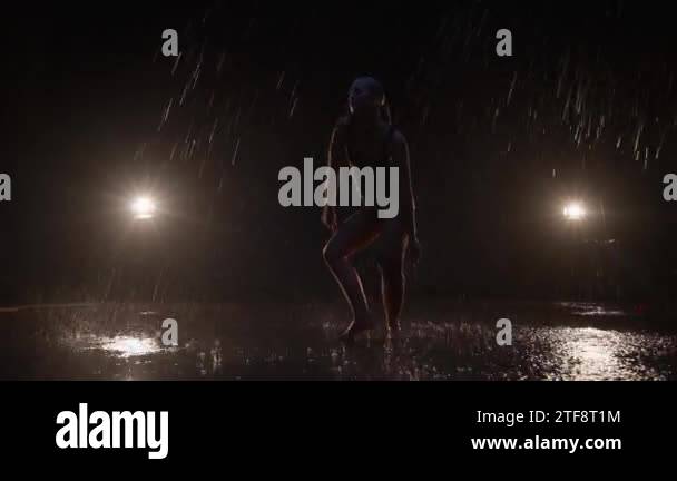 Sensual Young Woman Dancer Performing in the Rain in Dark Studio Against Black Backdrop and with ...