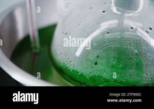 Boiling green liquid in the misted glass flask. The flask is in a bowl ...