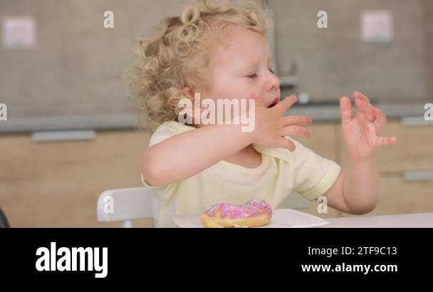 Adorable little girl licks her fingers after eating a donut, while ...