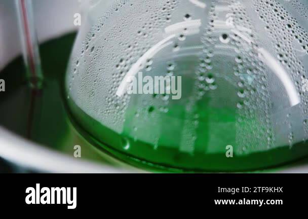 Misted glass flask with green liquid. Close-up. Drops flow down the ...