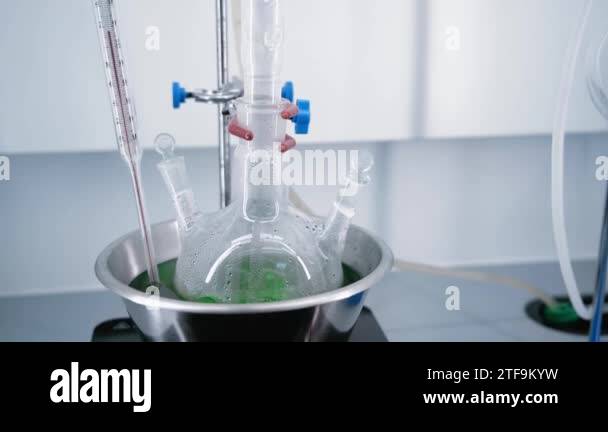Misted glass flask and thermometer in a bowl. Green liquid boils in the ...