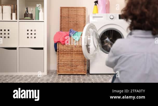 Happy causasian teen boy throwing dirty clothes into washing machine as ...