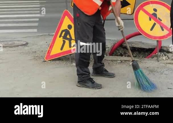 A municipal worker sweeps the road with a broom. Road signs. Road ...