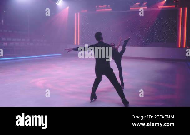 Figure skaters pair on ice rink in neon light skating by camera,man ...