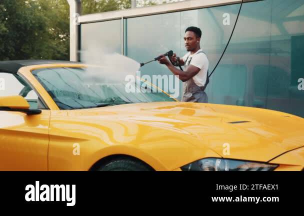 Manual car wash. Handsome African young man washing his luxury yellow ...