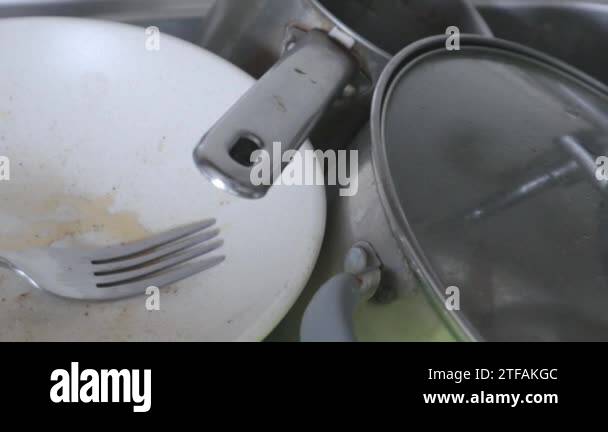 The kitchen utensils in the wash basin need to be washed. A pile of ...