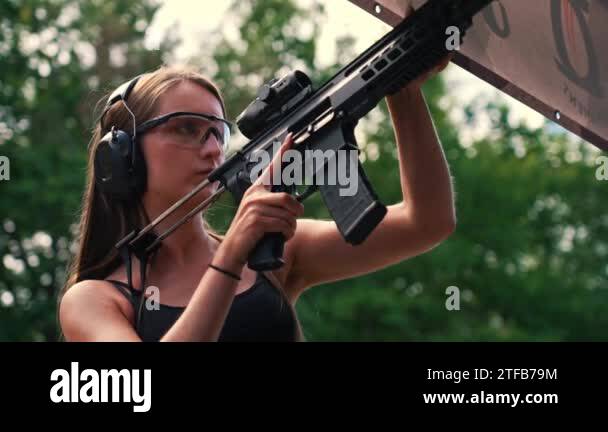 White brunette woman in protective gear firing submachine gun on ...