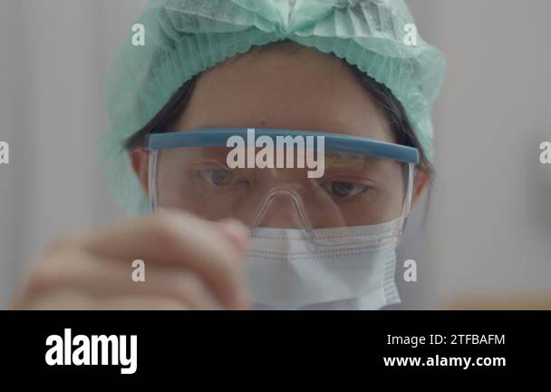 Asian female scientist wearing face mask holds test tube with a blood ...