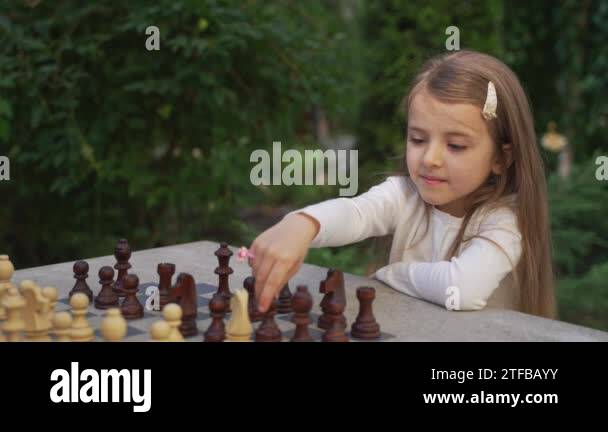 Close up cute little girl playing chess outdoor. Concentrated smart ...