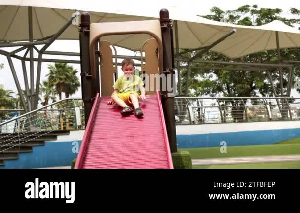 Child laughs happily, slides down childrens slide in childrens park ...