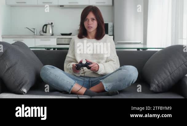 Beautiful excited young gamer girl sitting on a couch, playing and ...