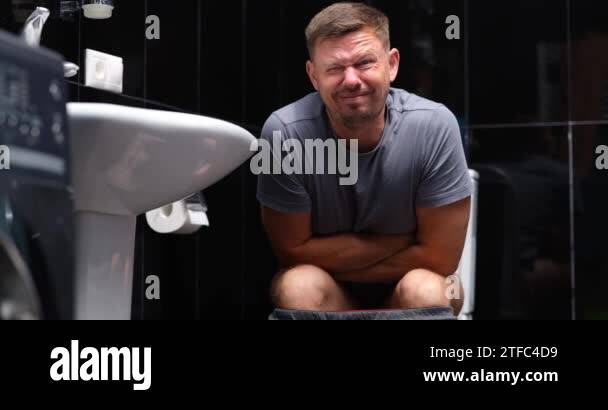 Young caucasian man suffering from hemorrhoids on toilet in toilet ...