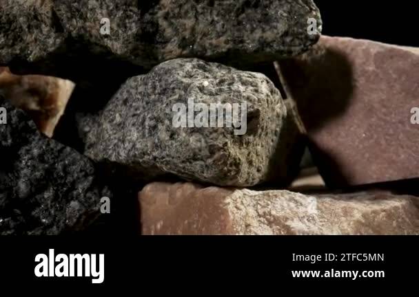 Pieces of solid rough granite stone rotating against a black studio background. Brown and gray ...