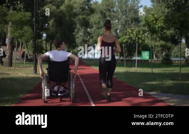 Live camera follows man rolling wheelchair as woman jogging on sports ...