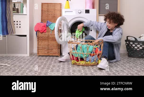 Young teen boy sits in front of a washing machine in Jeans Clothes. He ...