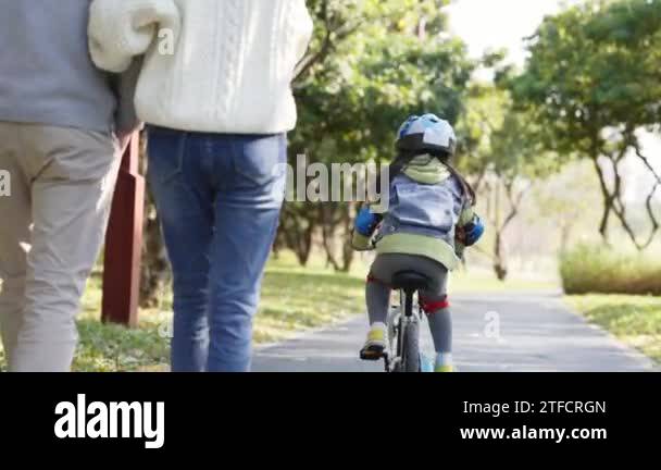 rear view of little asian girl riding bike with full protective gears ...