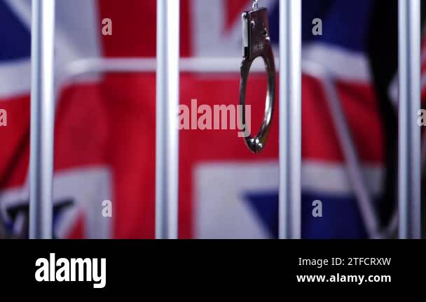 Handcuffs swing on prison bars with Union jack British flag background ...
