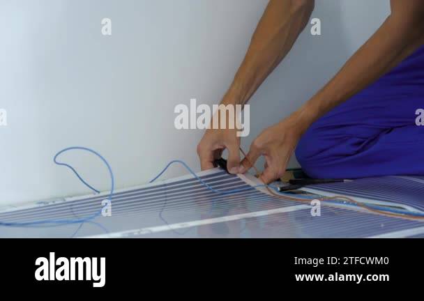 A professional master of underfloor heating installation connects the ...