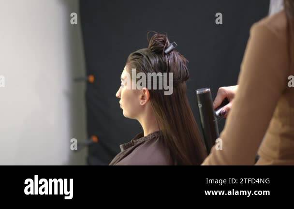 Side view woman rubbing nose as hairdresser drying hair in slow motion ...