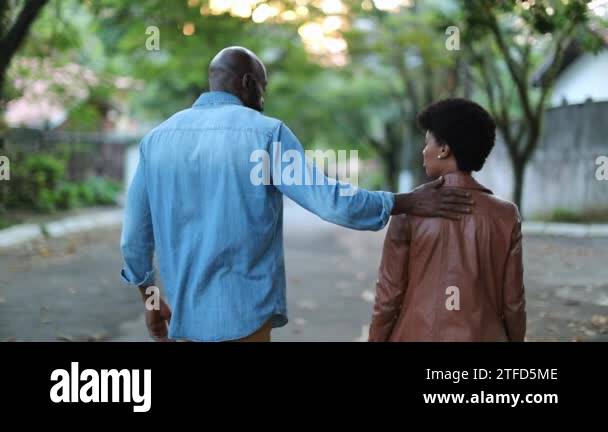 Back of two people walking together in street, man putting arm around ...