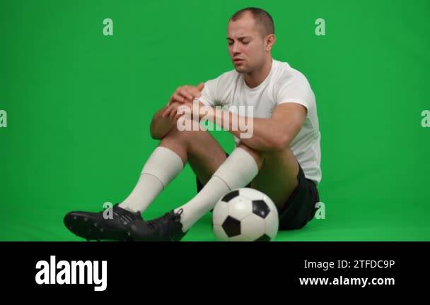 Desperate Caucasian footballer sitting with soccer ball on green screen ...