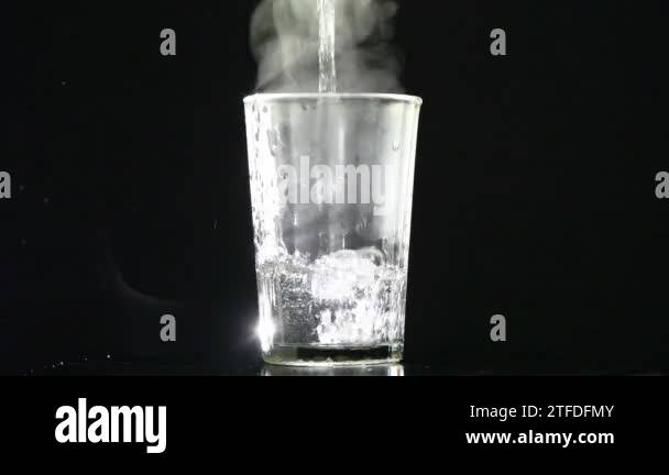 Boiling water is poured into a glass. Steam and bubbles are clearly ...
