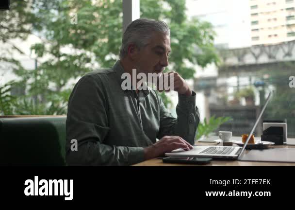 Middle aged man working at coffee shop in front of laptop. Older person ...