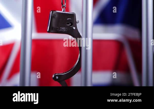 Handcuffs swing on prison bars with Union jack British flag background ...