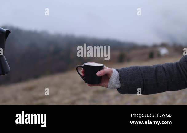 A person pouring out coffee from Moka pot into a cup outdoors in front ...
