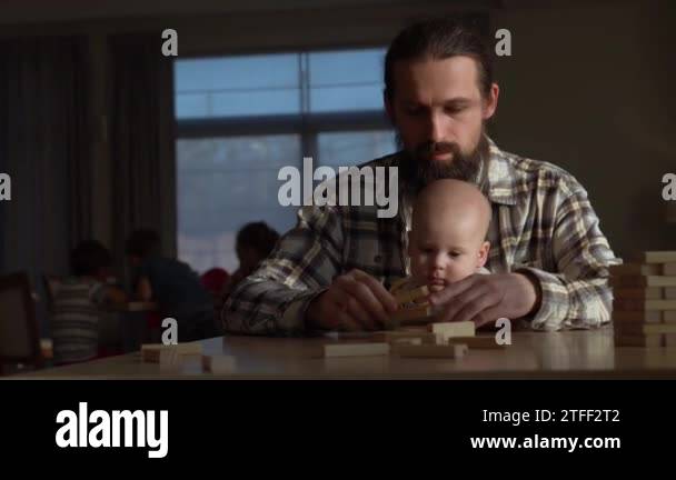 Small Kid newborn with Dad playing tiny jenga her parents at table ...