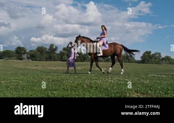 Young twin sisters walking on horseback by green field at countryside ...