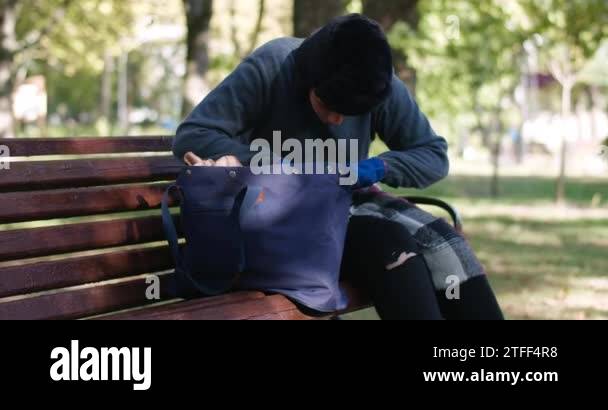 Focused homeless young woman rummaging in bag in slow motion sitting on ...