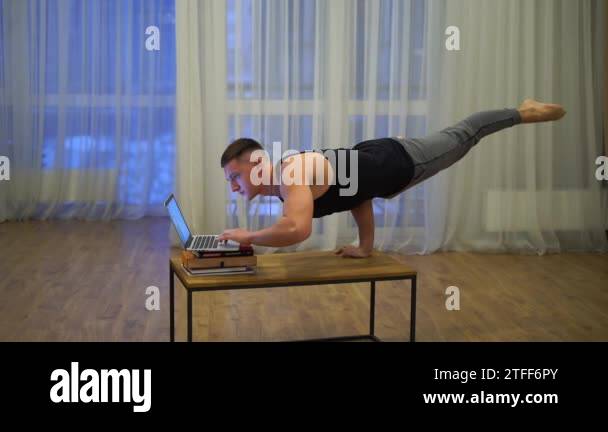 A muscular man keeps balance on one hand and uses laptop. Self ...