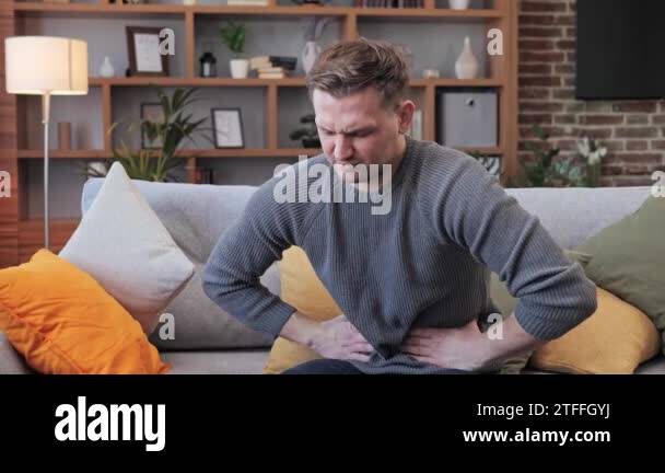 Man sitting on the couch at home, suddenly feeling strong stomach ache ...