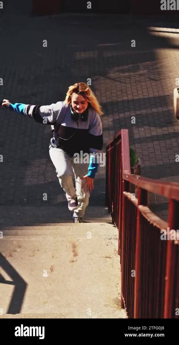 Vertical, caucasian teen blonde girl happily running up stairs ...