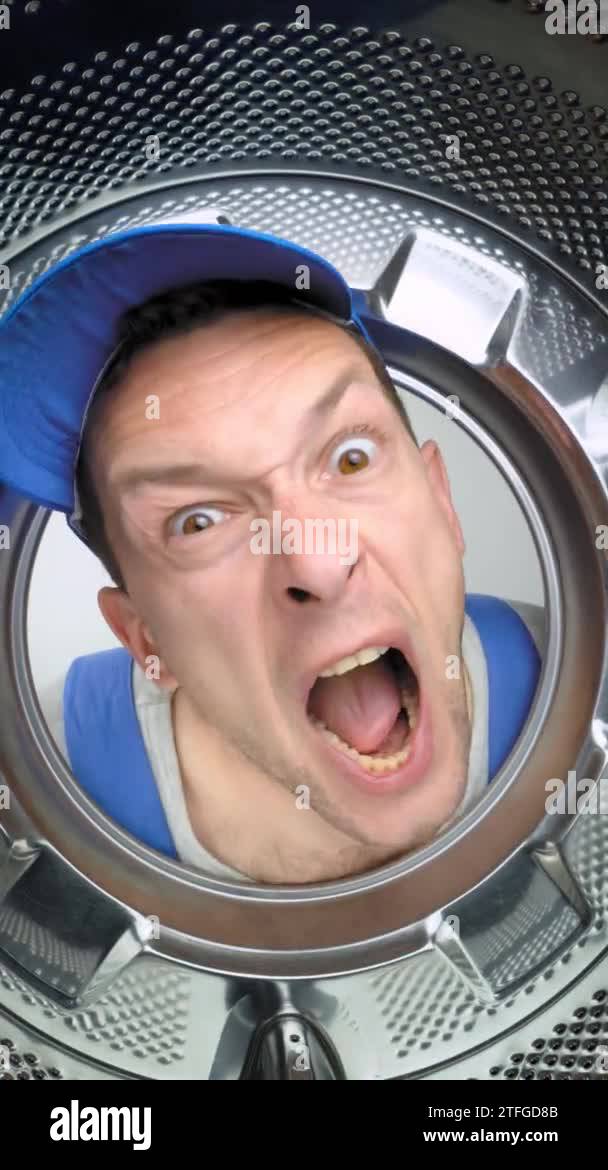 a home appliance repairman in blue uniform sticks his head into drum of ...